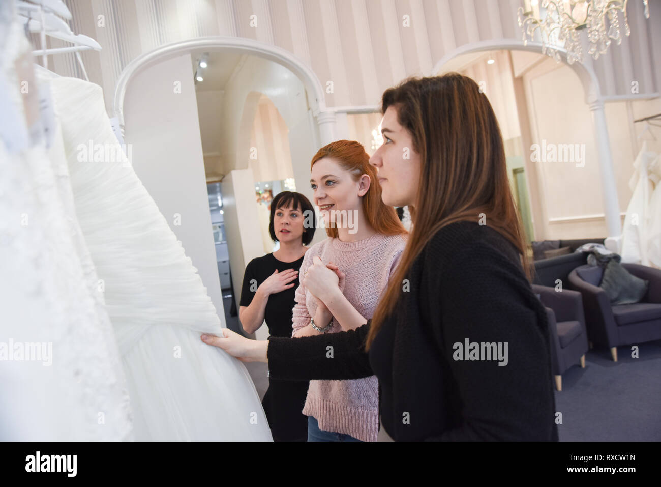 2 shop assistants are helping a pretty red haired girl in a Wedding ...