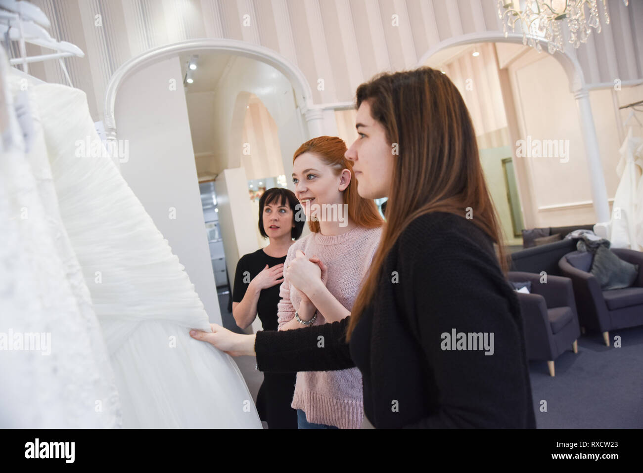 2 shop assistants are helping a pretty red haired girl in a Wedding ...