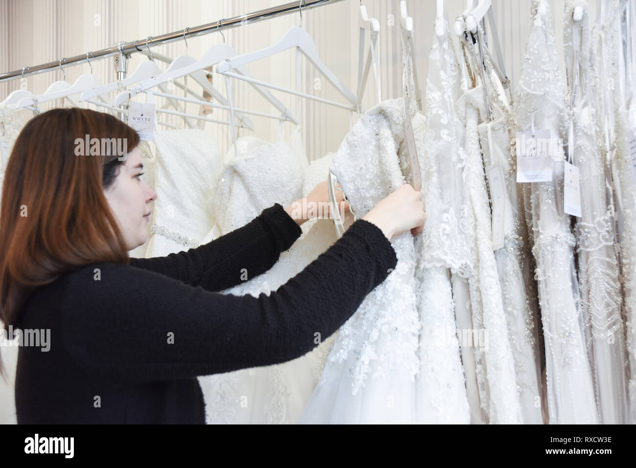 A young female shop assistant is selecting dresses in a Wedding dress ...