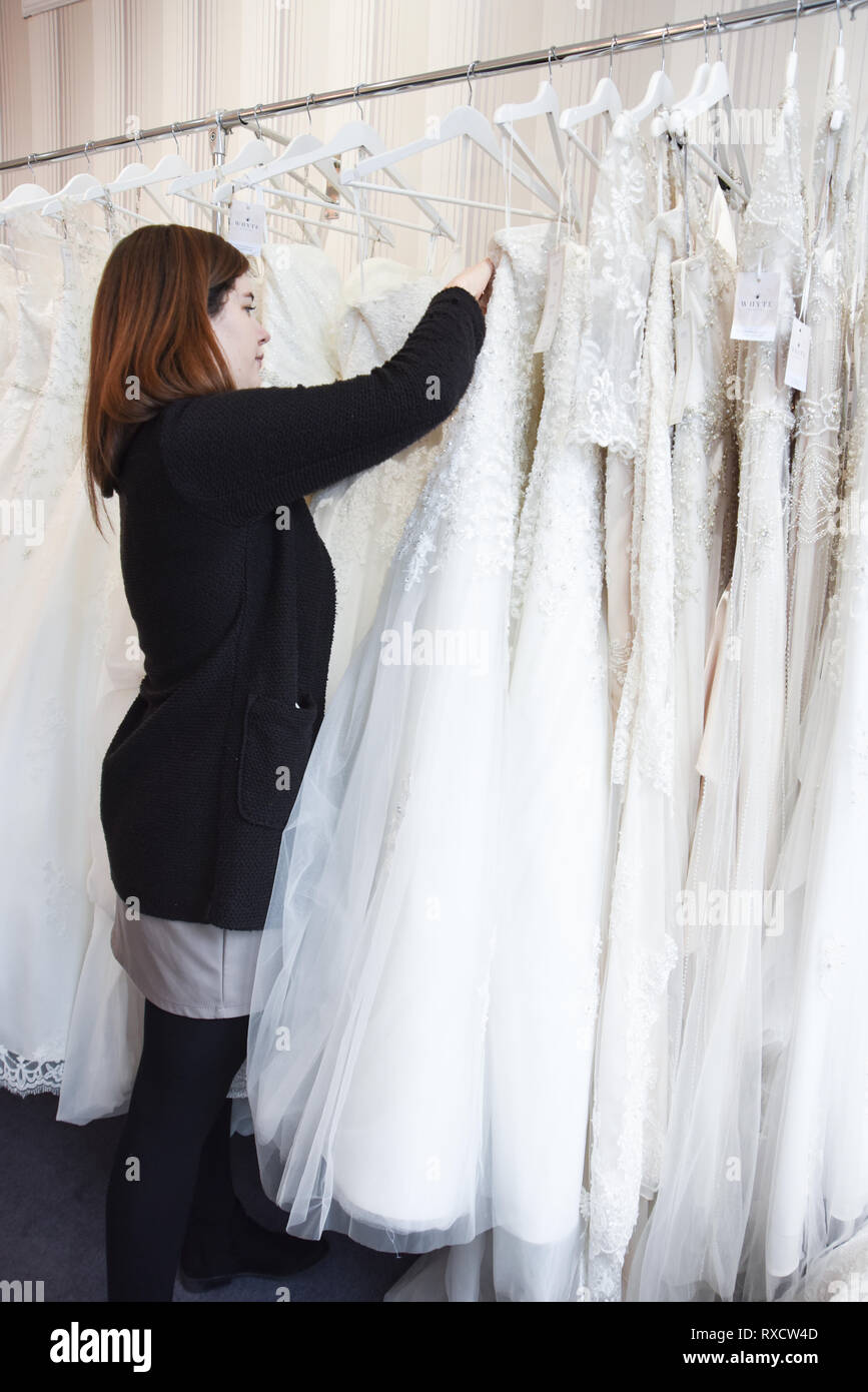 A young female shop assistant is selecting dresses in a Wedding dress ...