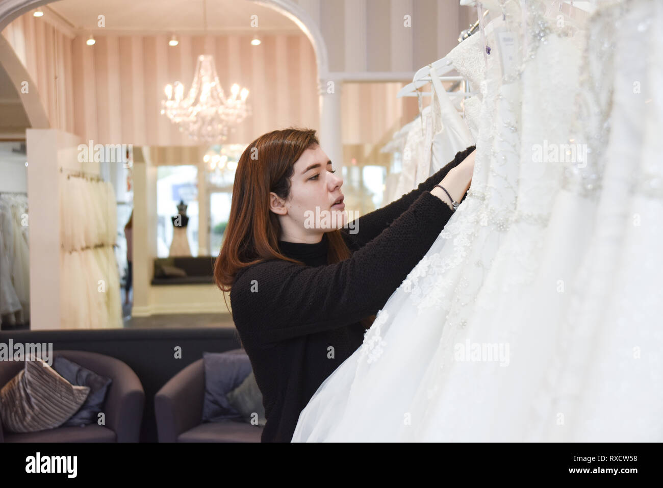 A young female shop assistant is selecting dresses in a Wedding dress ...