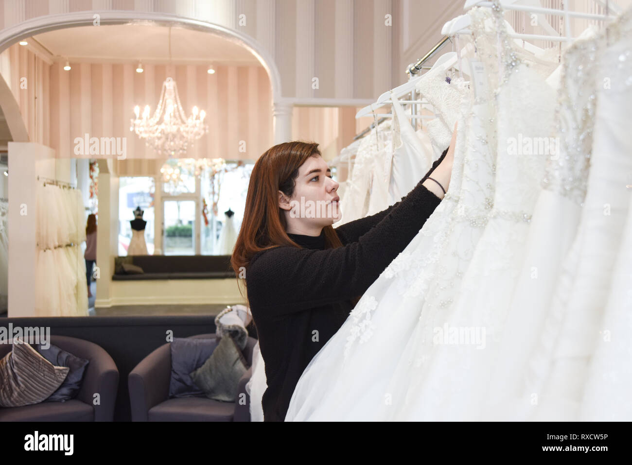 A young female shop assistant is selecting dresses in a Wedding dress ...