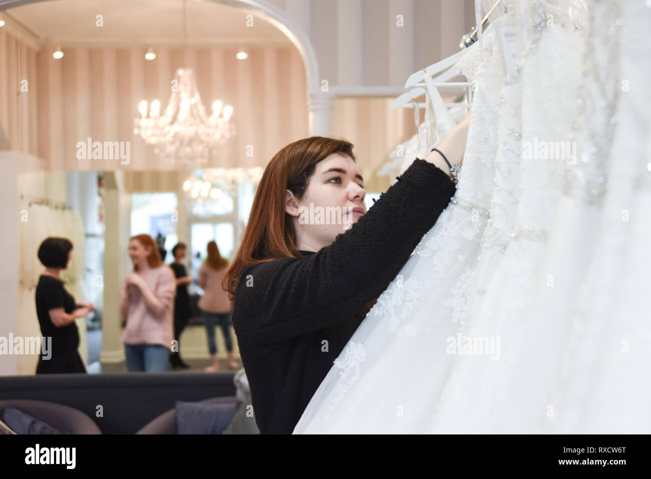2 shop assistants are helping a pretty red haired girl in a Wedding ...