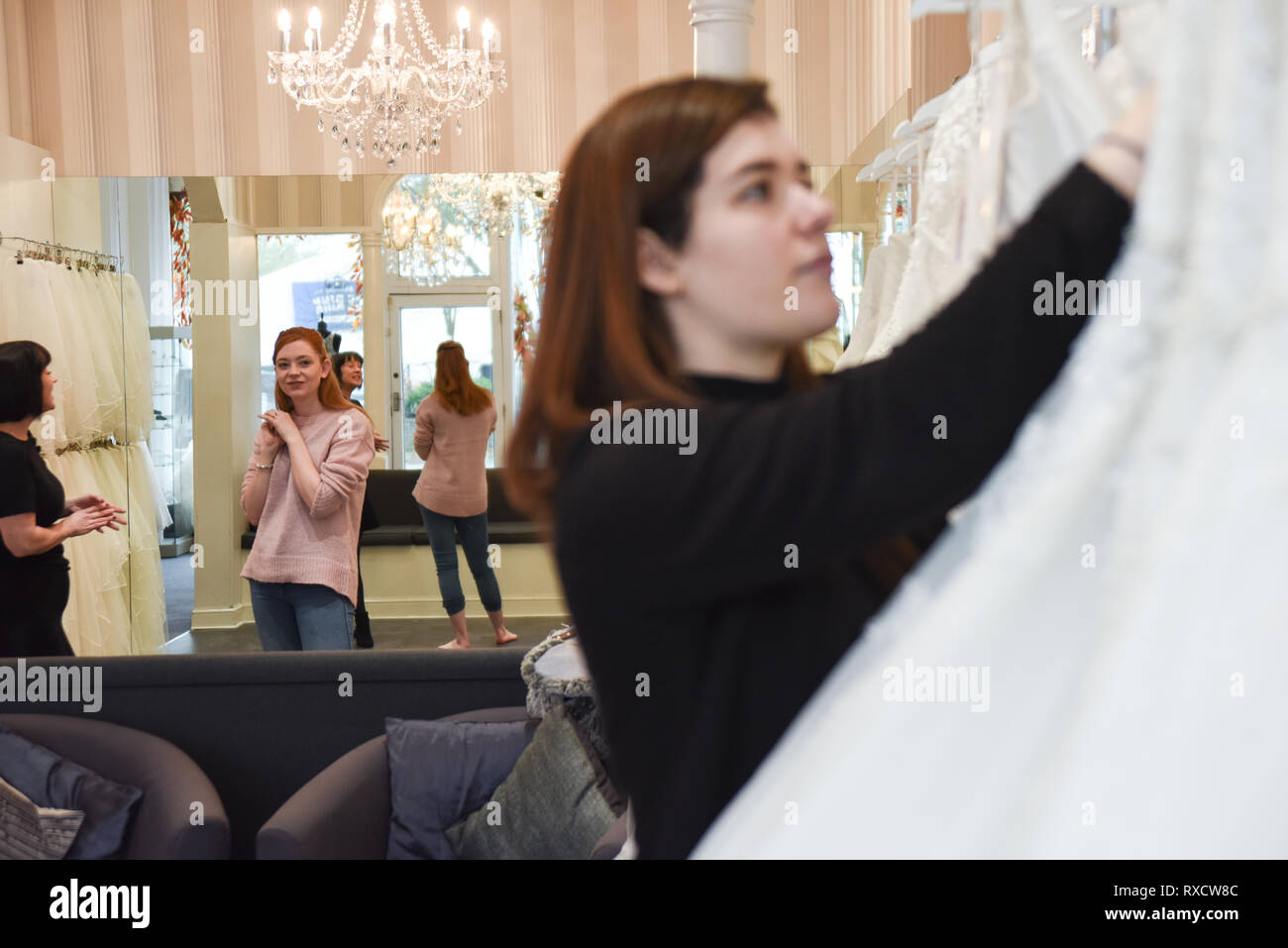 2 shop assistants are helping a pretty red haired girl in a Wedding ...