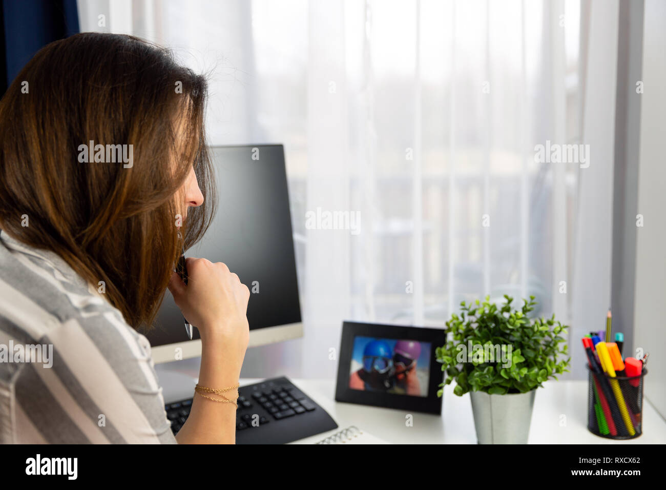 Young woman manager sitting and thinking in workspace with computer and ...