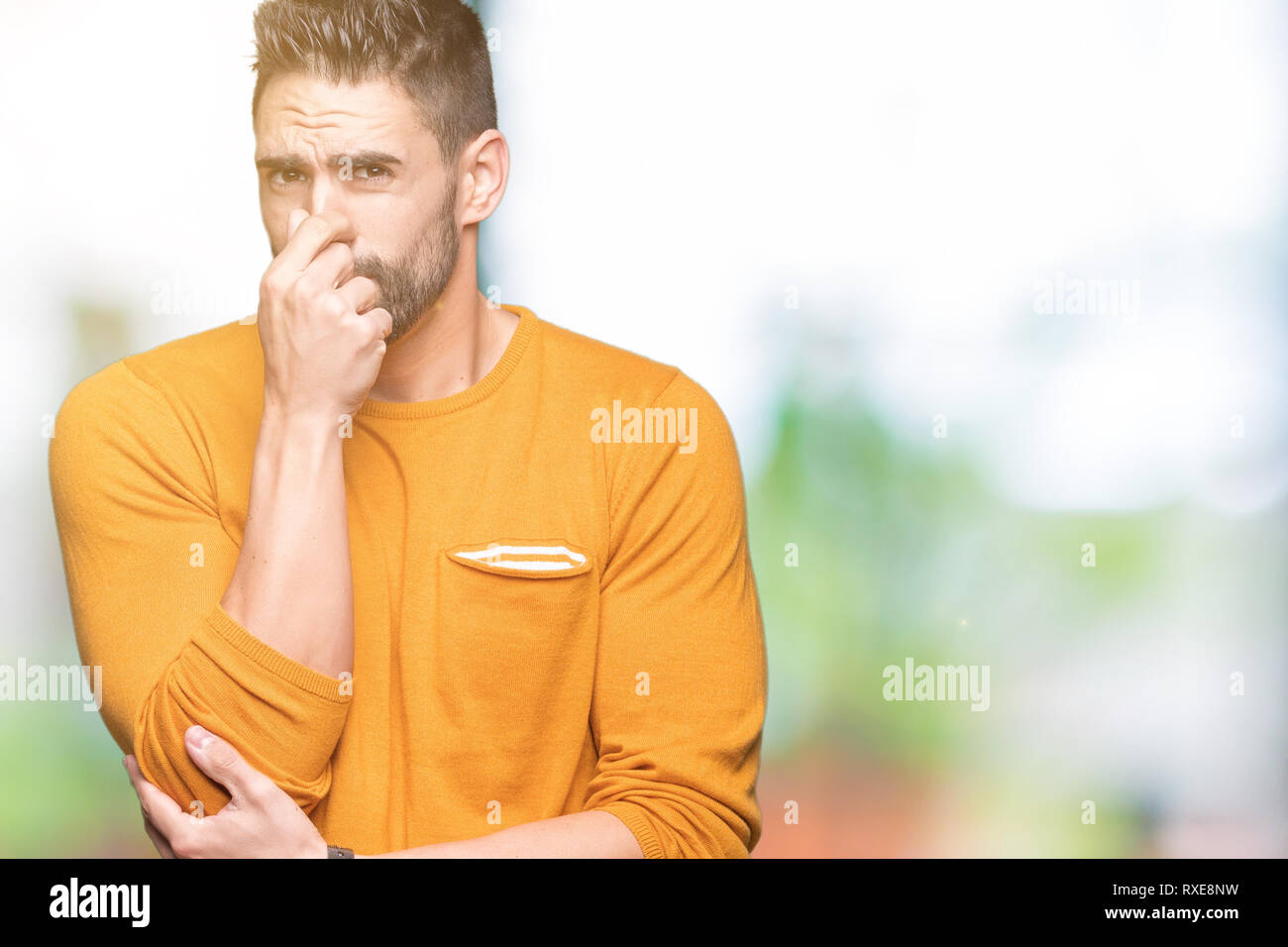 Young handsome man over isolated background smelling something stinky ...