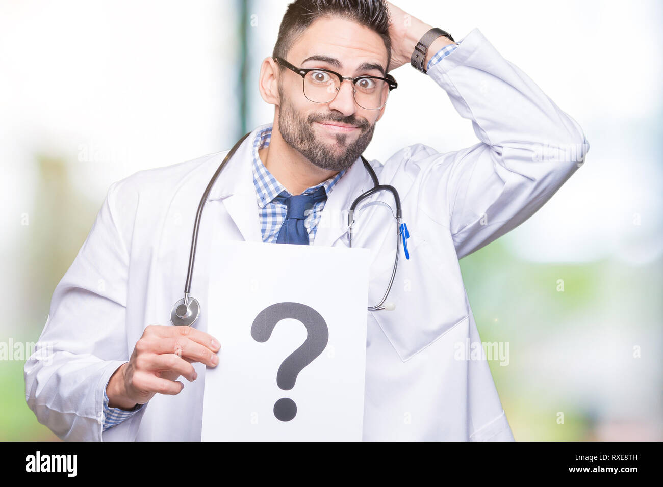 Handsome young doctor man holding paper with question mark over ...