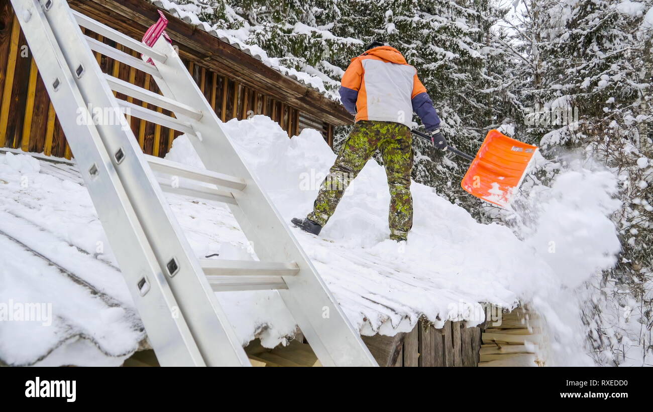 The man uses the ladder to climb off the roof. The man shovels the ...