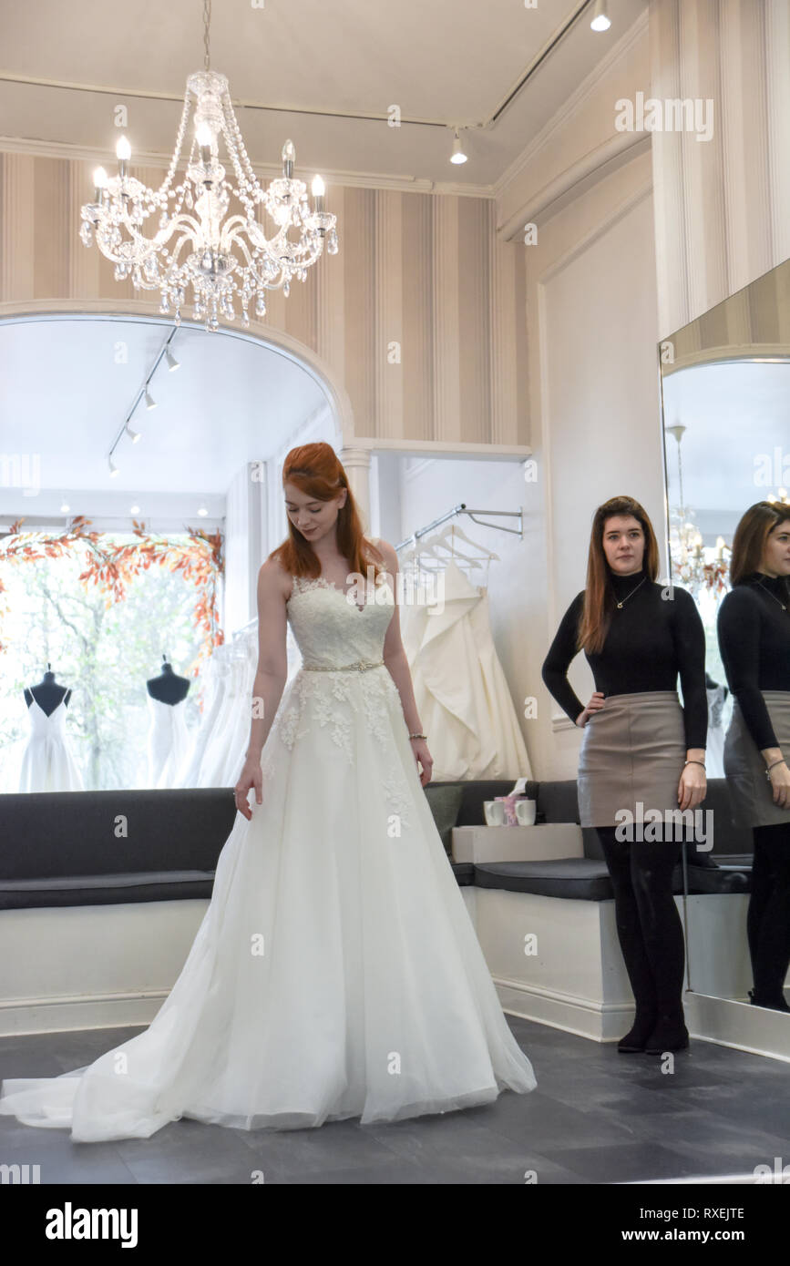 A pretty red haired girl is in a Wedding dress shop choosing & trying ...