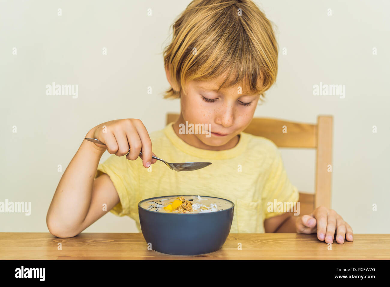 Happy boy sitting and eating a fresh smoothie bowl with mango, dragon ...