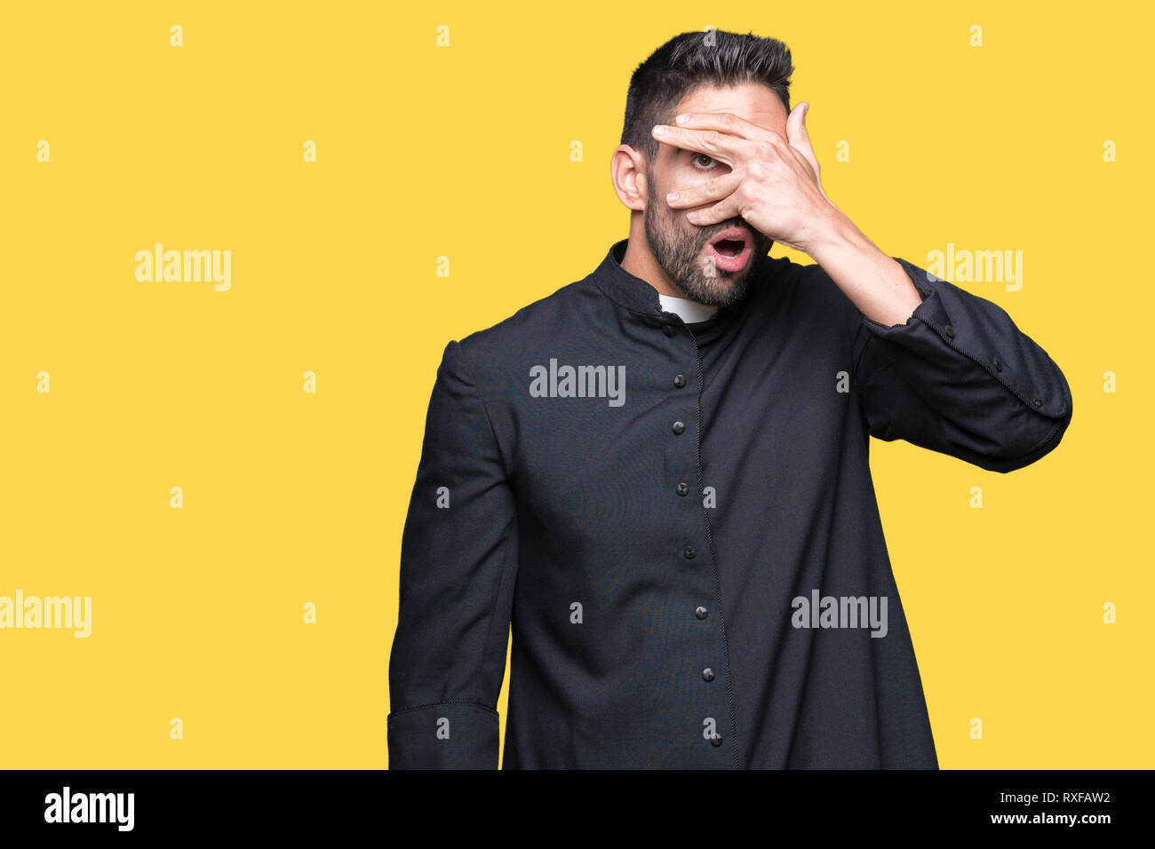 Young Christian priest over isolated background peeking in shock ...