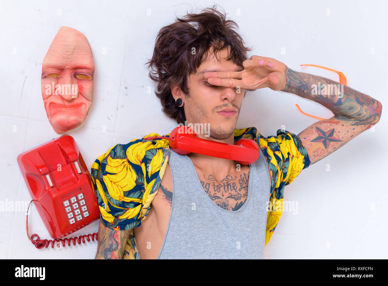 Young rebellious man lying on the floor with mask and telephone as ...