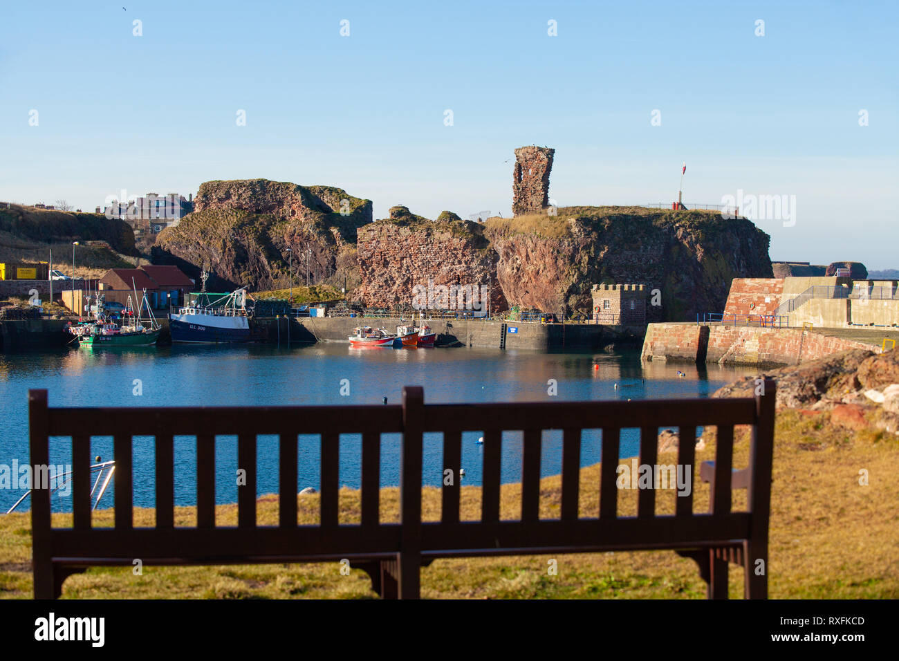 Dunbar harbour and Dunbar Castle with park bench in the foreground ...