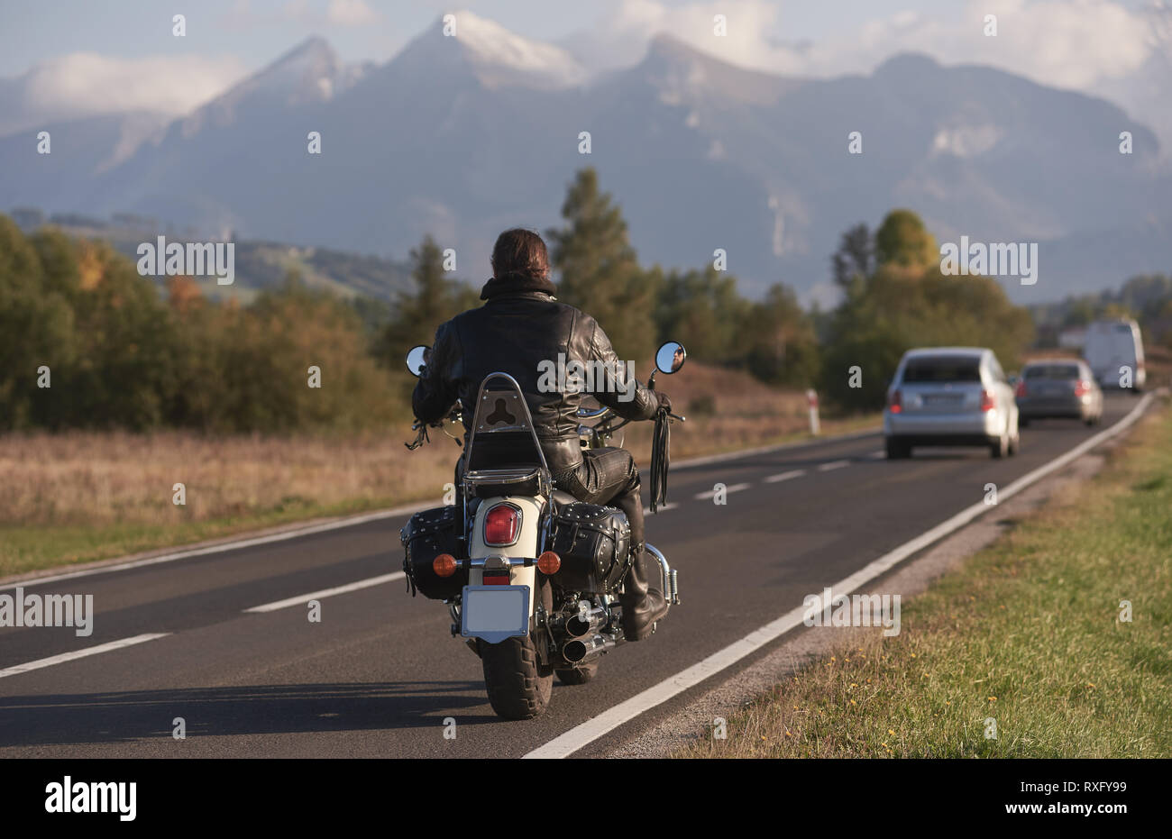 Back view of biker in black leather jacket riding motorcycle along road ...