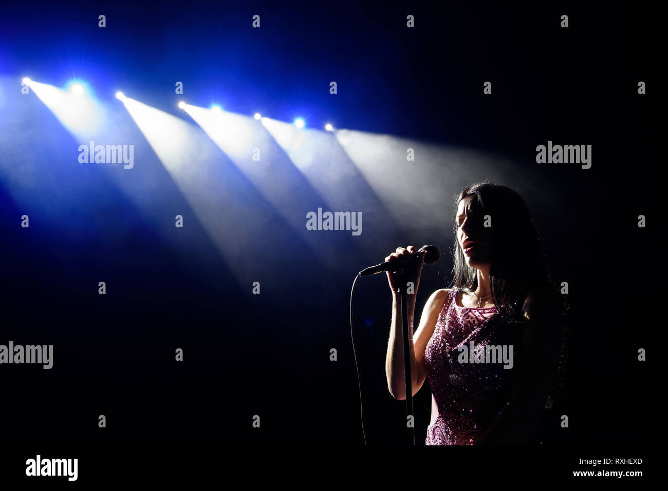 Shadow of singer in light. Portrait of beautiful singing woman on dark ...