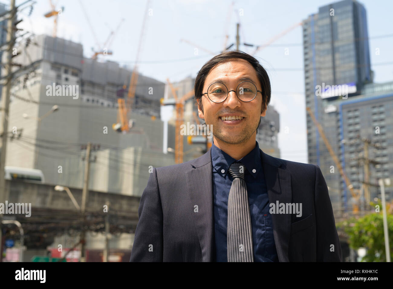 Face of happy Asian businessman smiling against view of construction ...