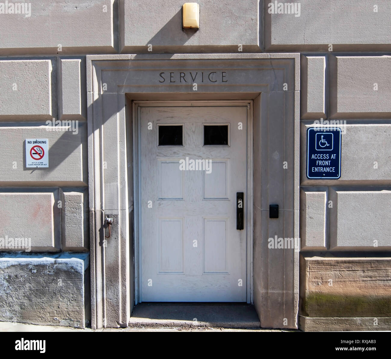 A white metal door in a doorway marked SERVICE in bright sunlight in ...