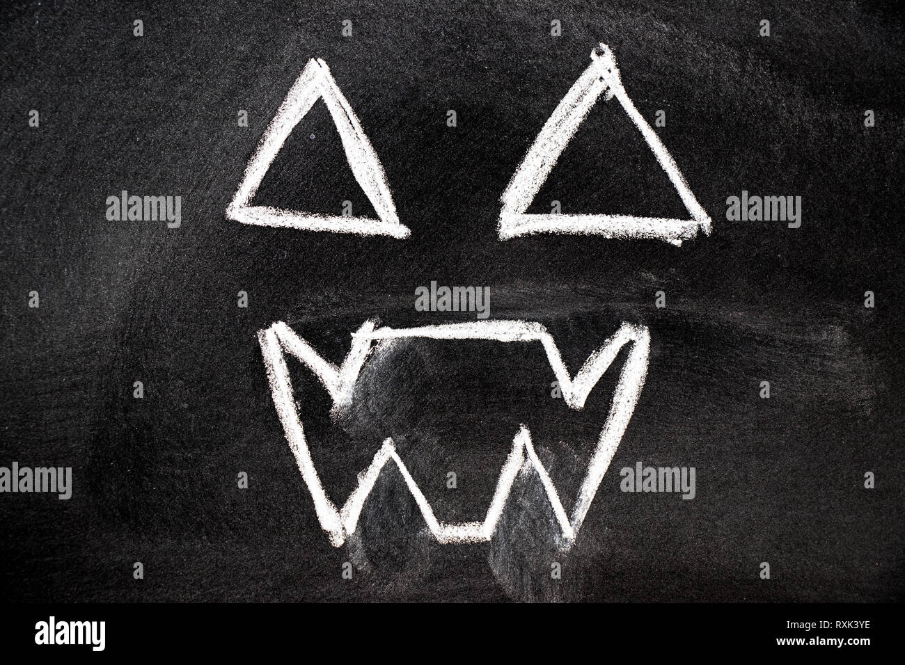 White color chalk hand drawing in ghost face shape on blackboard ...