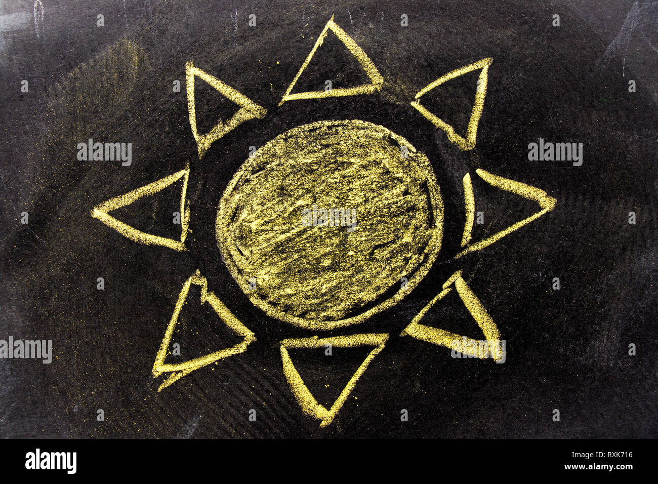 Yellow color chak hand drawing in sun with ray shape on blackboard ...