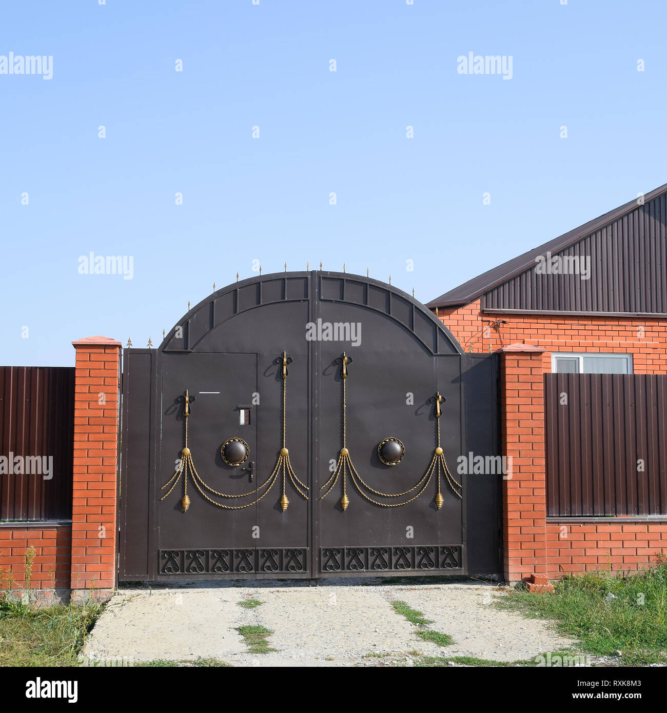 Brick house with a fence and gates. View of a new built-up fence and a ...