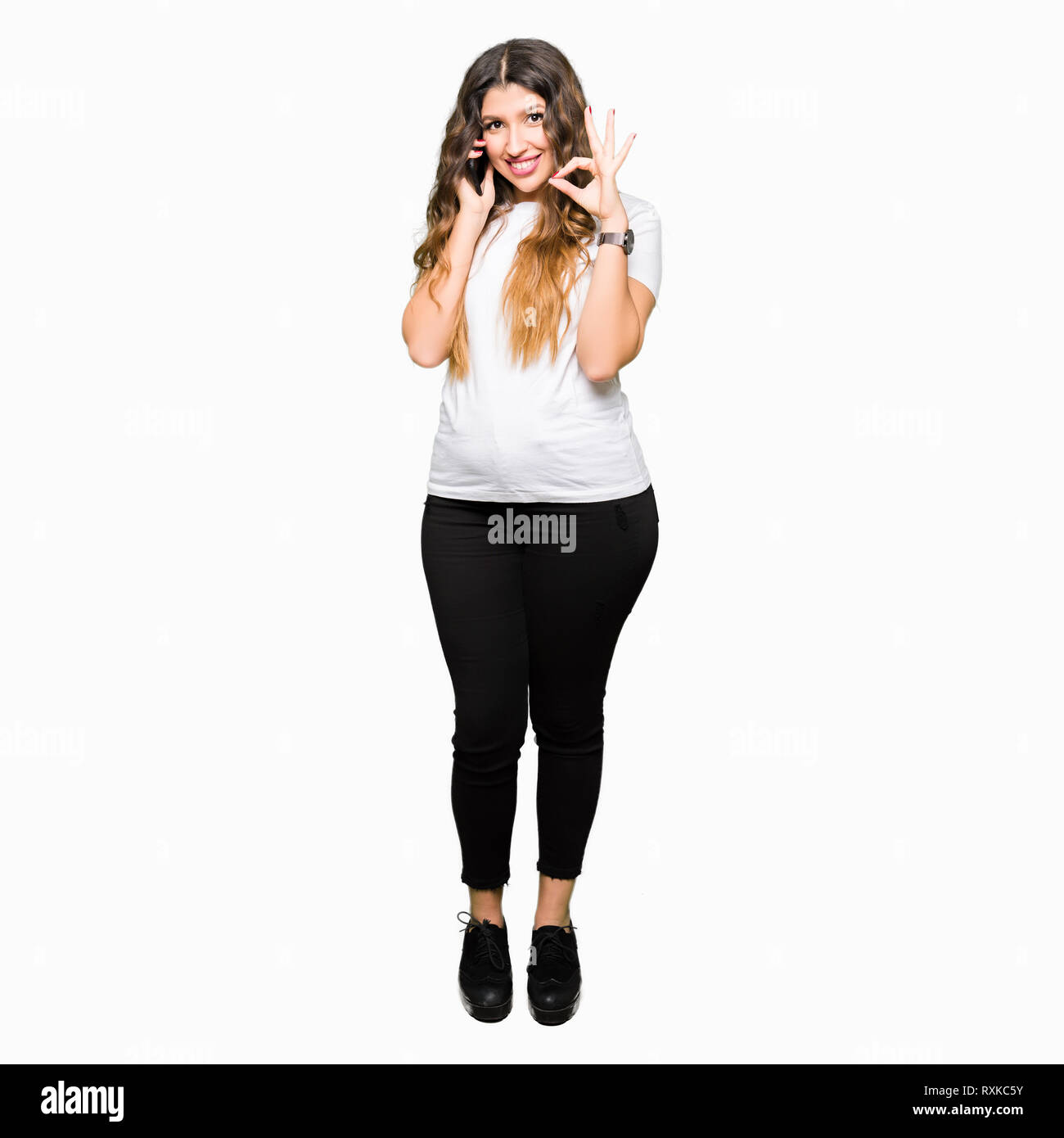 Young adult woman taking on the phone doing ok sign with fingers ...