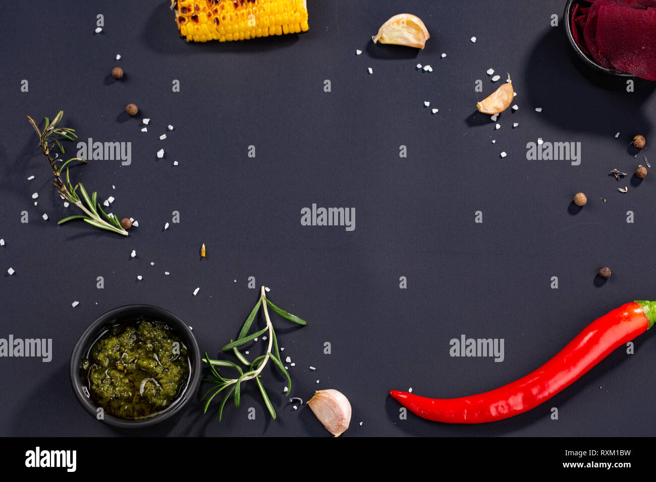 Black Culinary background with grilled corn, sauce, chilli, rosemary ...