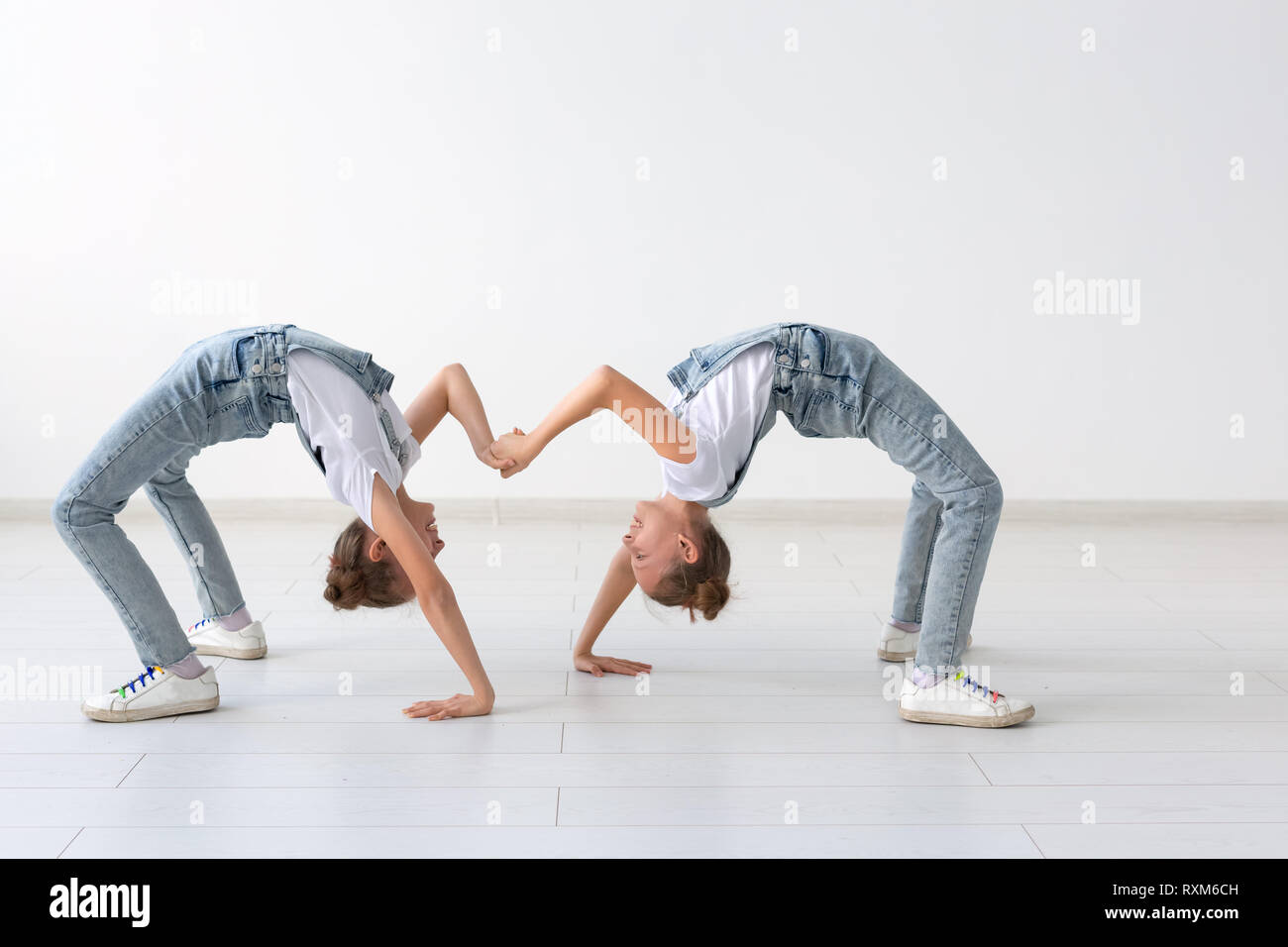 Family and sport concept - Two acrobat twin girls are standing on the ...