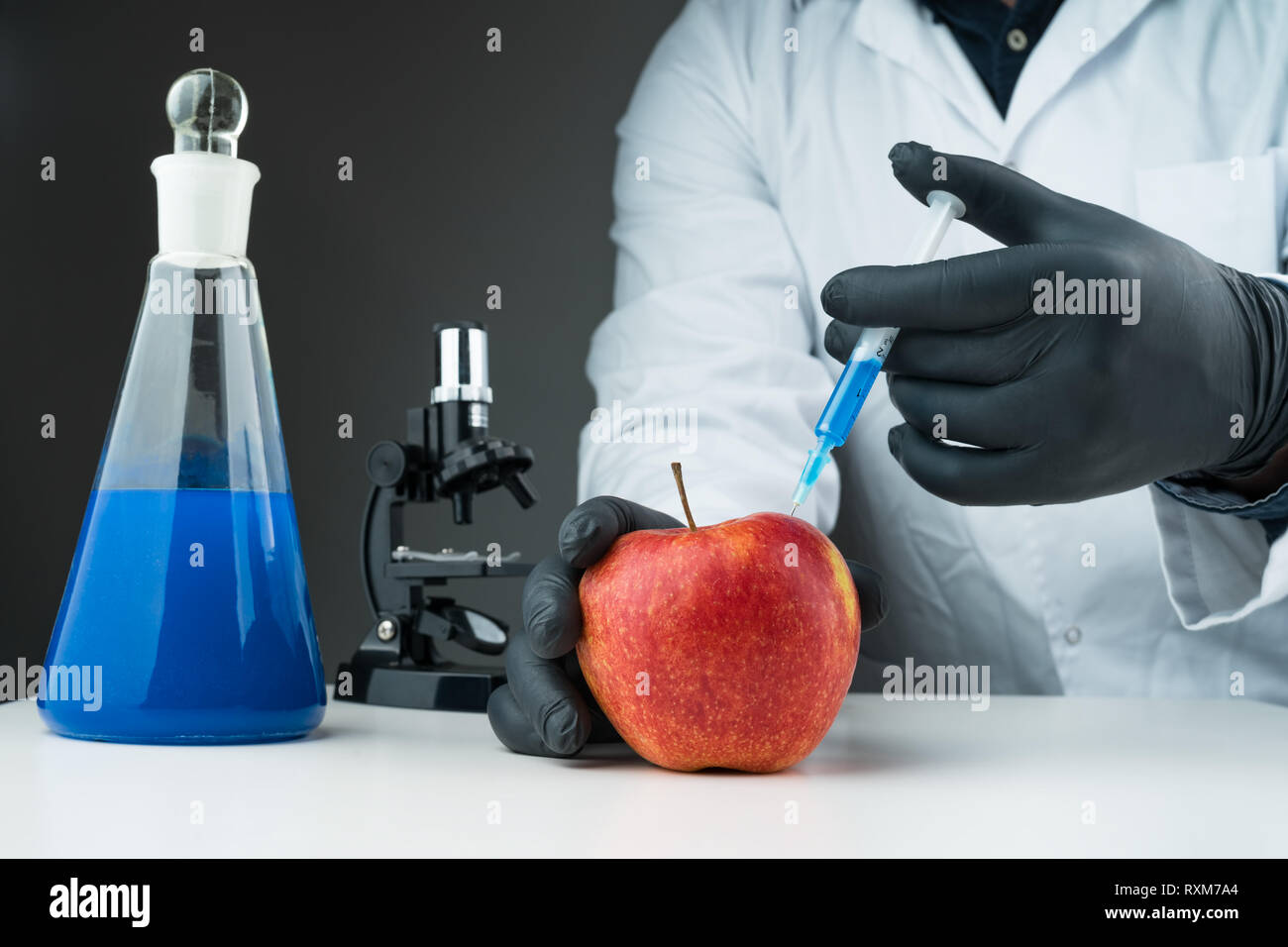 Young scientist using blue liquid, apple, syringe and microscope on a ...