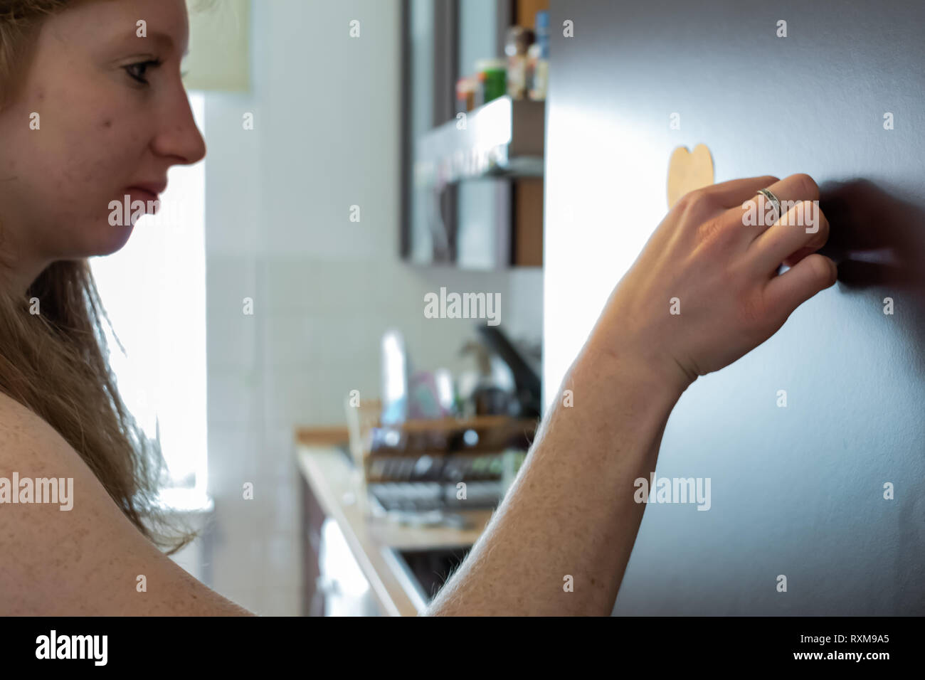 Side view of woman sticking a generic reminder note to the refrigerator ...