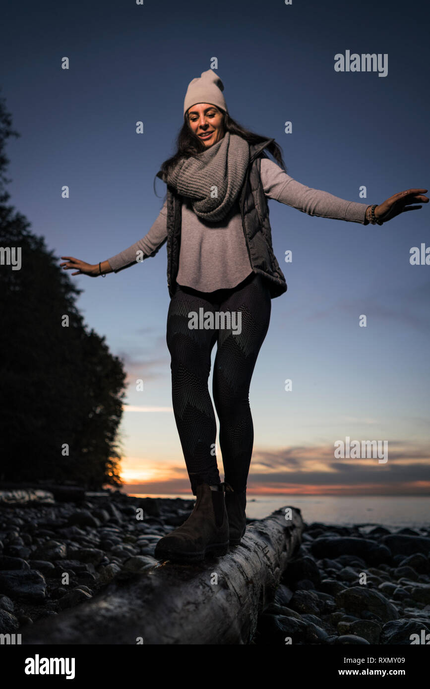 A female balances on a log at sunset, Acadia Beach, UBC, Vancouver, BC ...