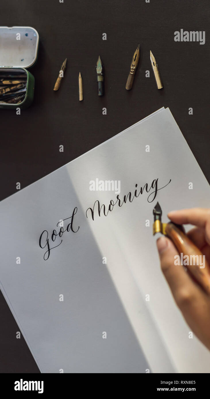 Calligrapher hands writes phrase on white paper. Phrase - Good morning ...
