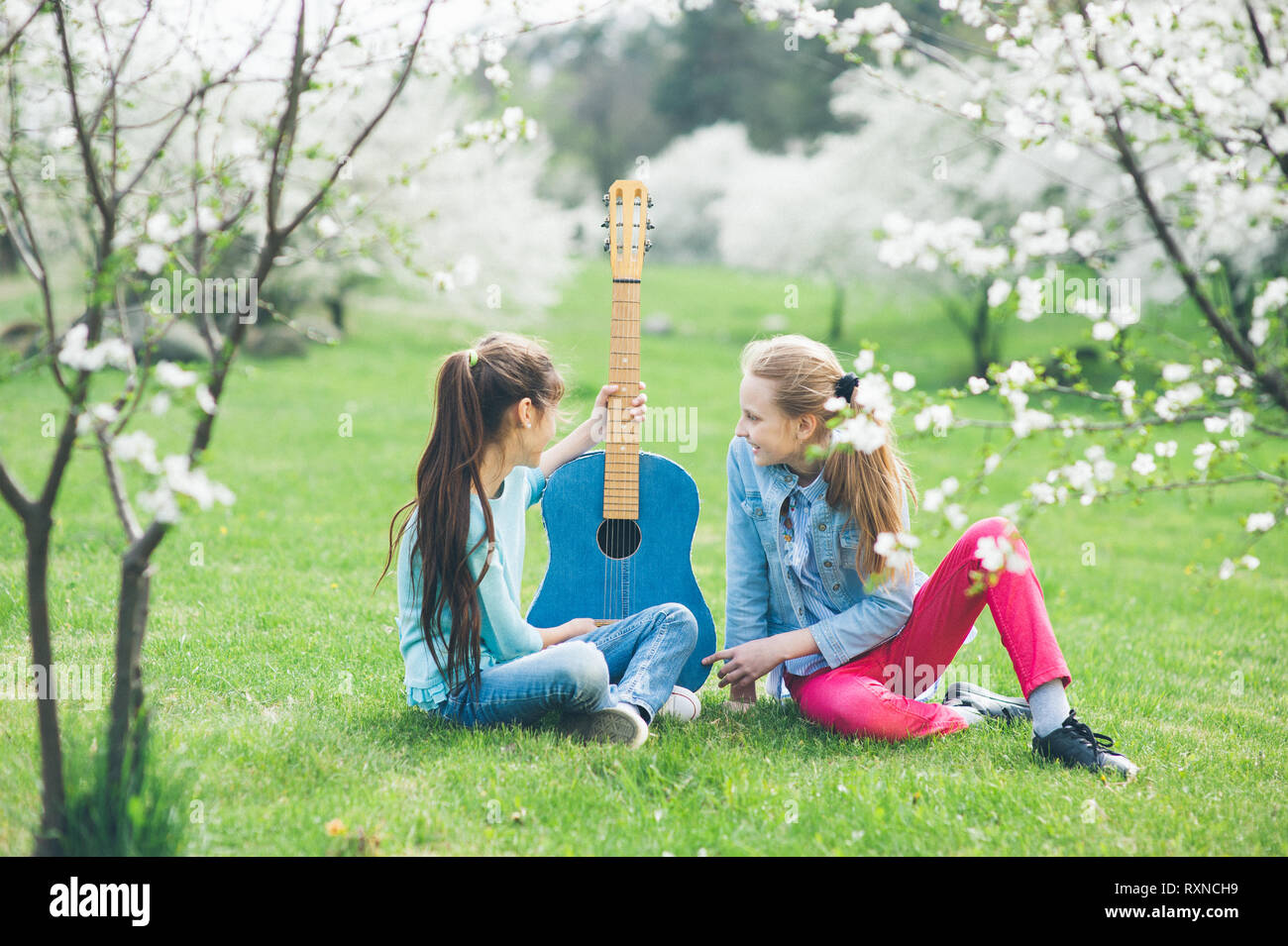 two happy friends young girls sitting on green grass together looking ...
