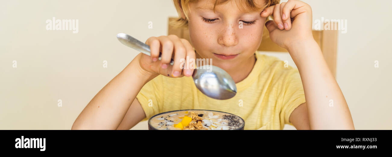 Happy boy sitting and eating a fresh smoothie bowl with mango, dragon ...