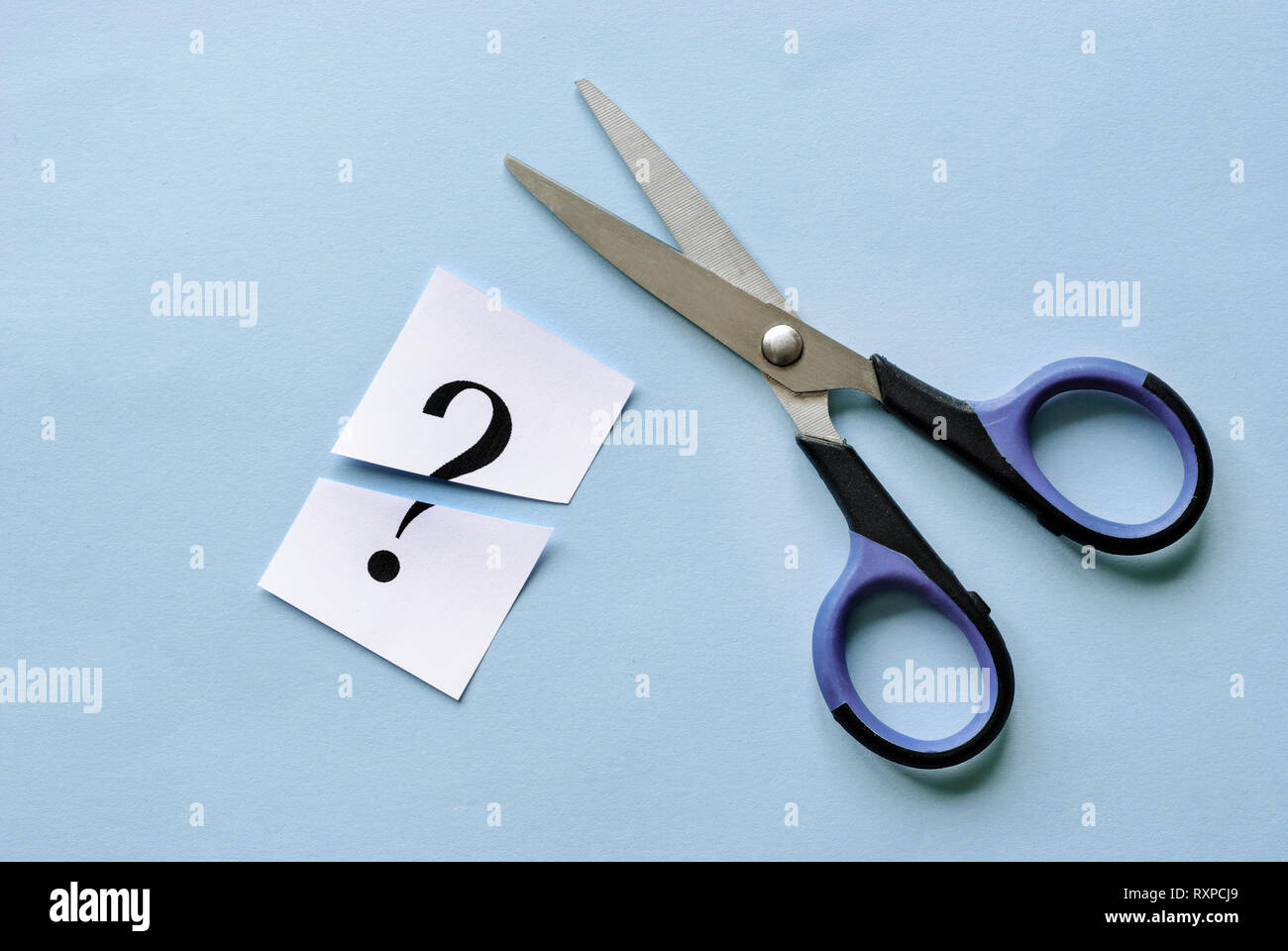 Question mark on a white card cut through with a pair of blue household ...