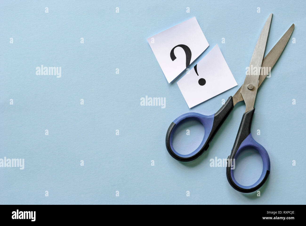 Question mark on a white card cut through with a pair of blue household ...