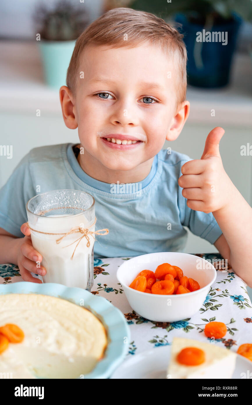 Beautiful little boy eating breakfast and drinking milk in kitchen at ...