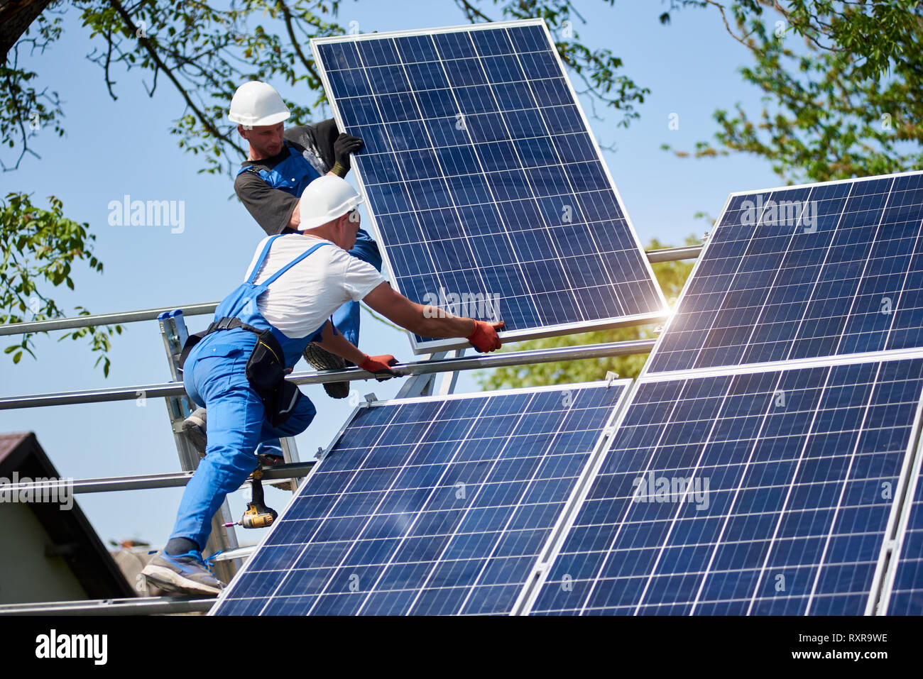 Two workers mounting heavy solar photo voltaic panel on tall steel ...