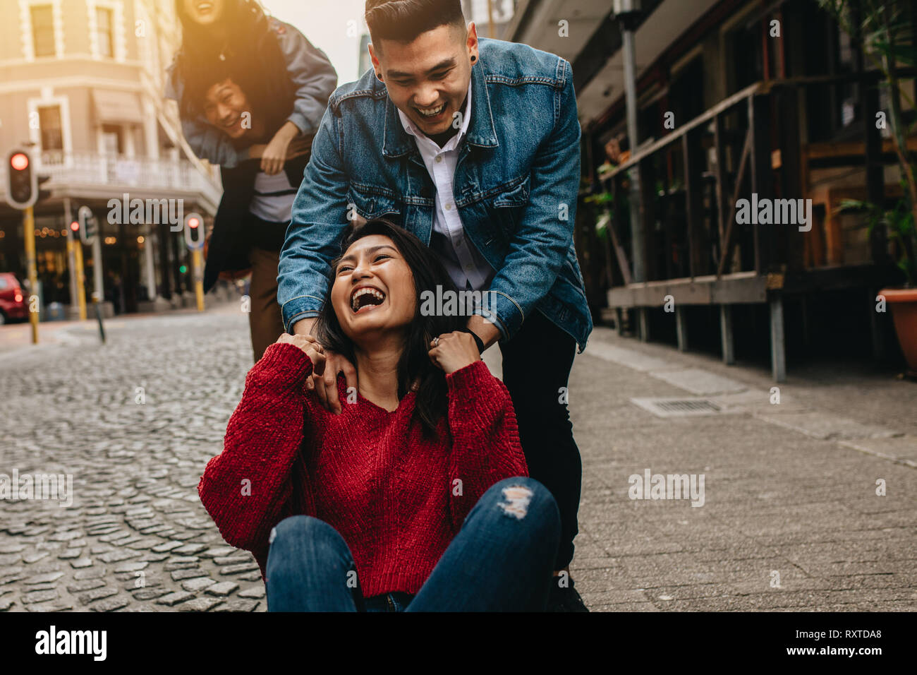Excited young woman being pushed on skateboard by her boyfriend ...