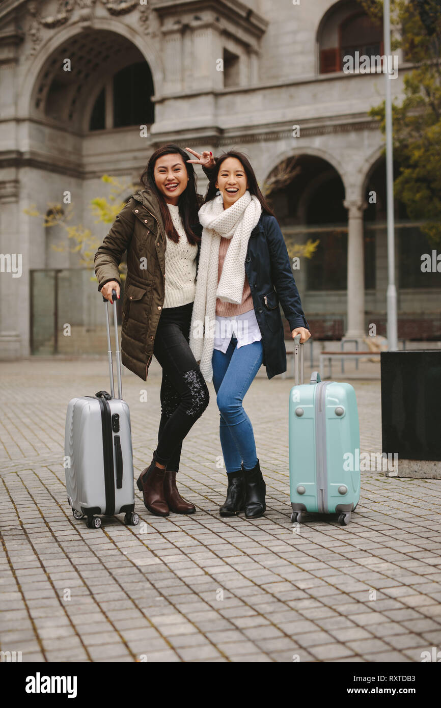 Two female tourists standing in street holding their luggage bags and ...