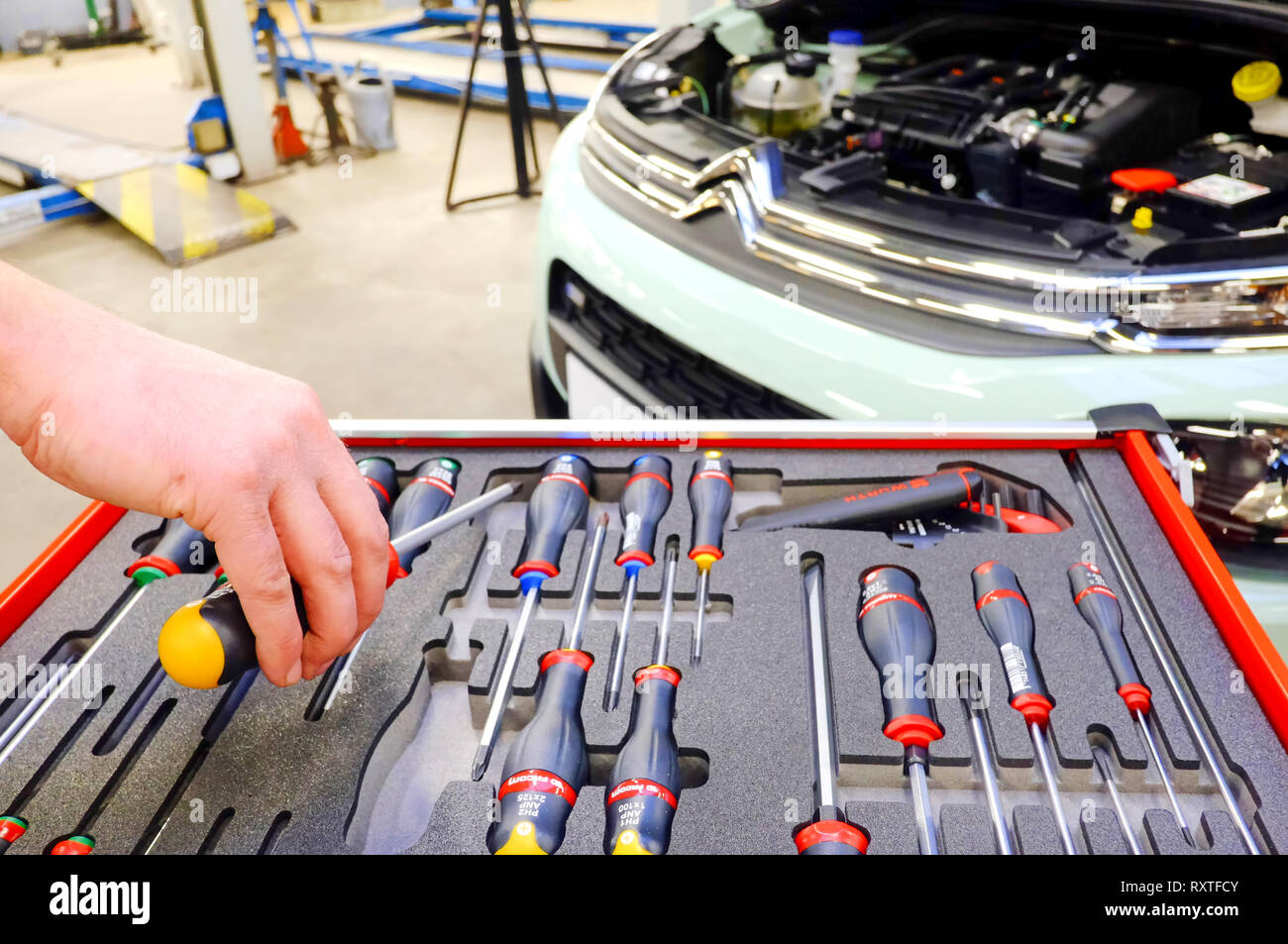 Auto mechanic picks tools from his toolbox in the background a car with ...