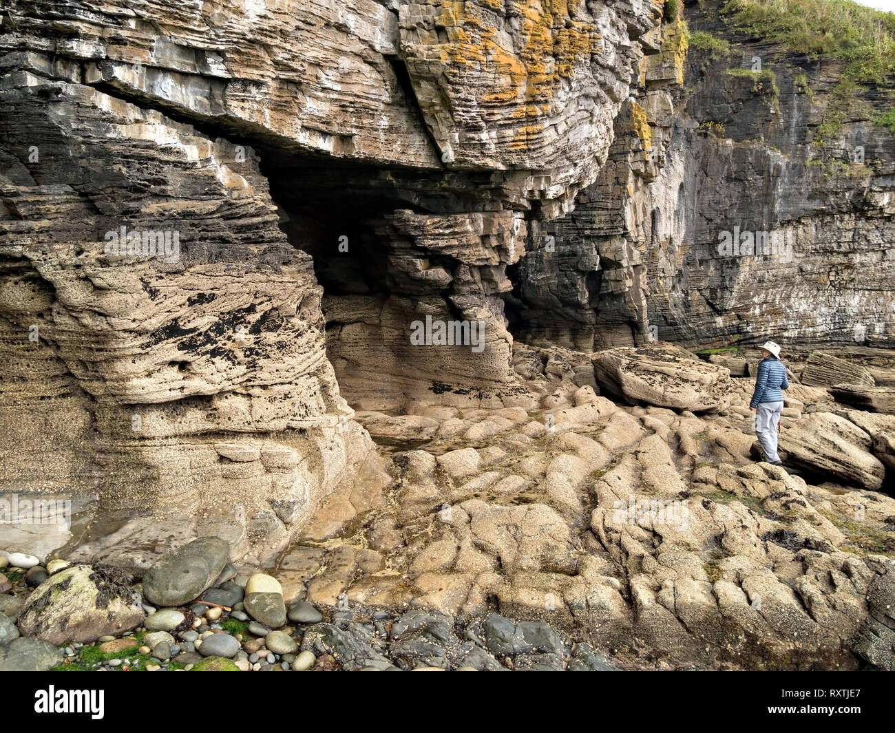 Female tourist looking at eroded rocks sea cliffs and sea caves on ...