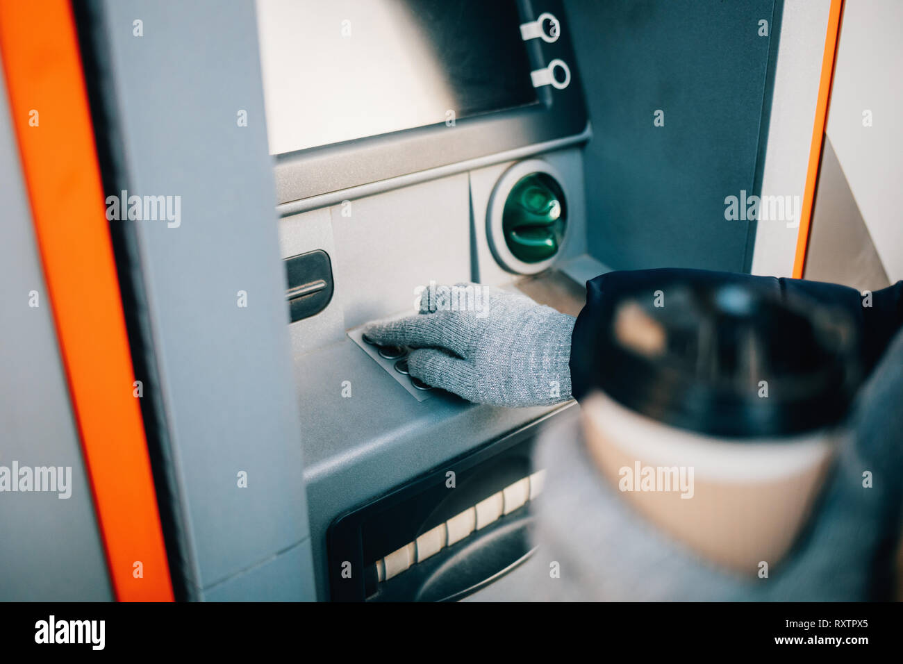 Close-up of young woman's hands holding coffee and entering PIN on ATM ...