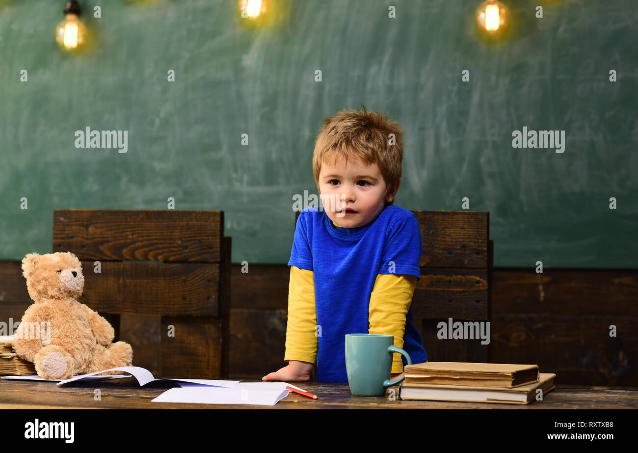 Small boy with serious face standing behind dark wooden table ...