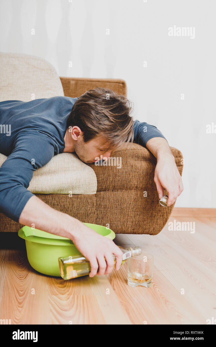 Alcoholic man lying on couch and pouring whiskey from bottle to glass ...