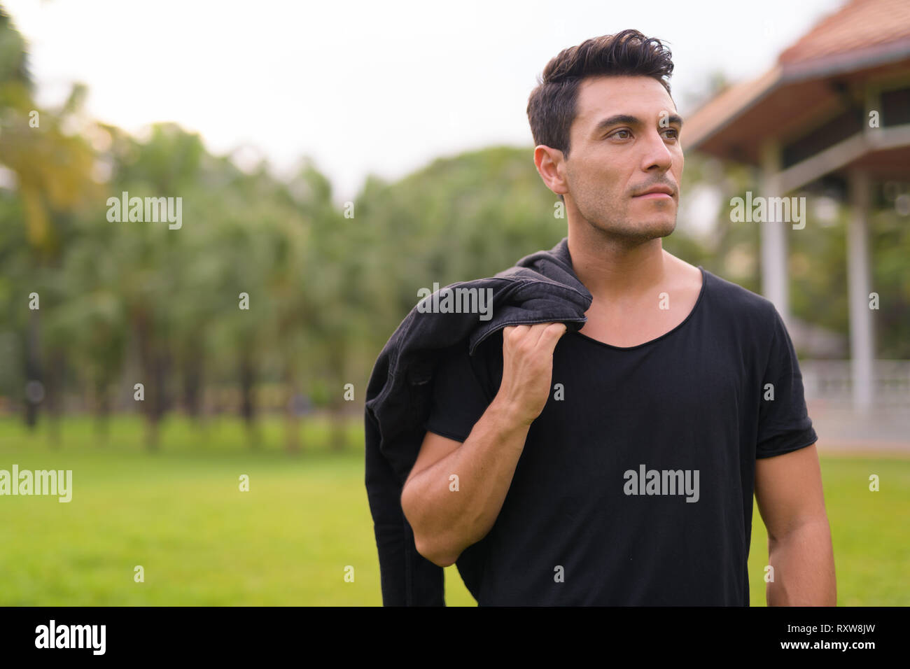 Young thoughtful Hispanic man carrying jacket over shoulder at the park ...