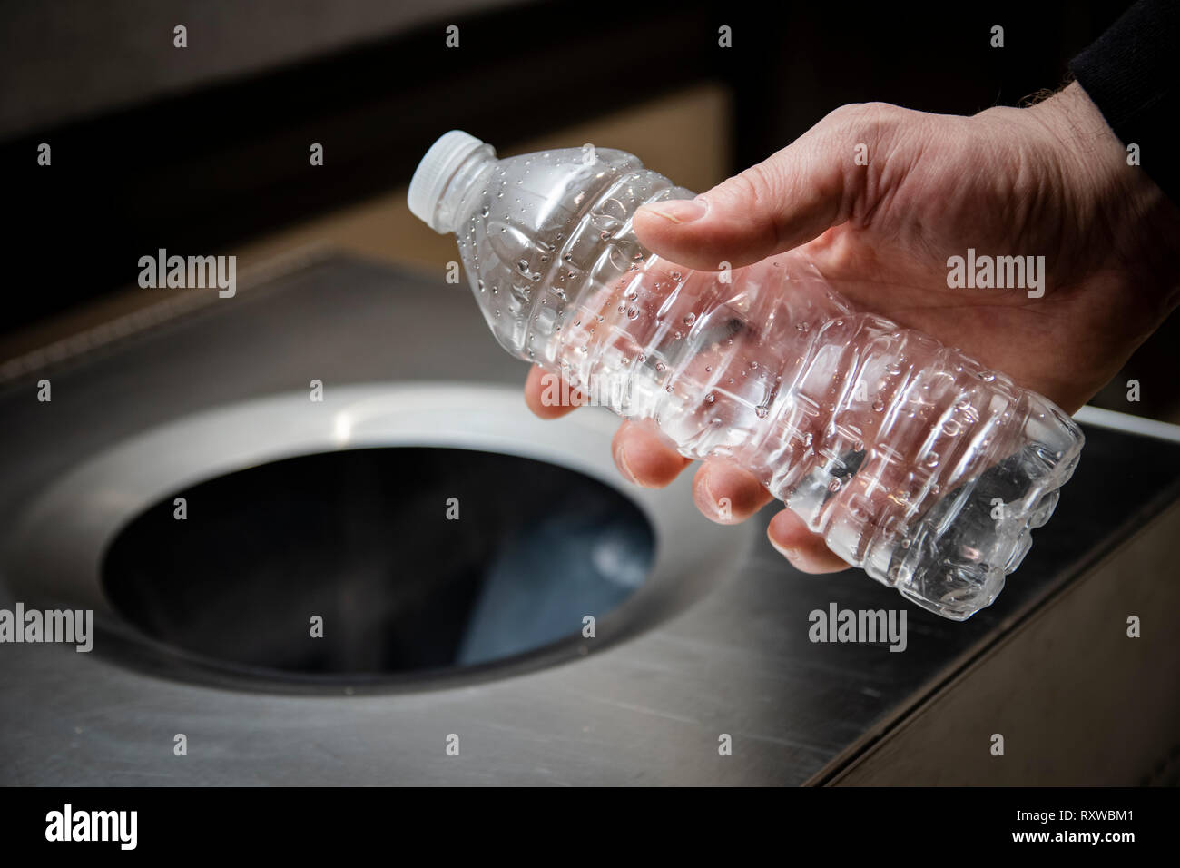 Hand throwing disposable plastic water bottle into trash or recycling ...