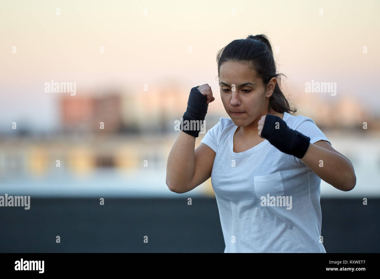 Young girl fighter shadow boxing on roof with buildings in background ...