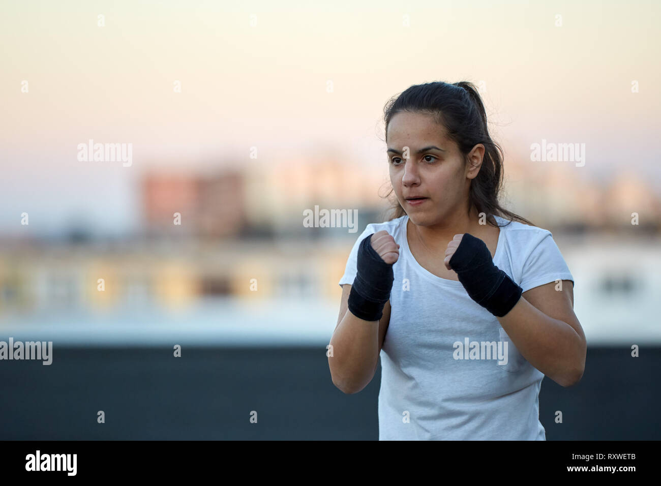 Young girl fighter shadow boxing on roof with buildings in background ...