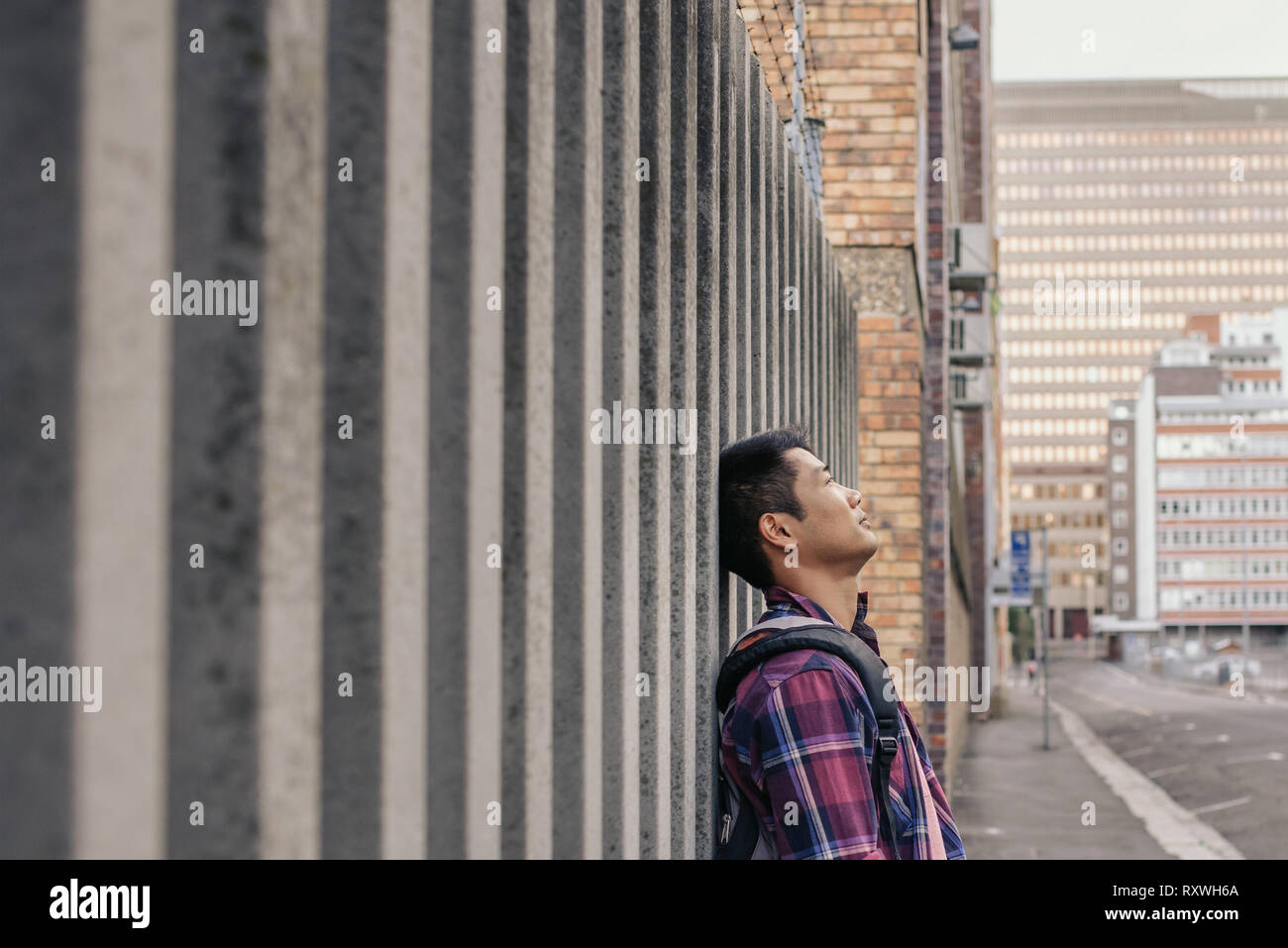 Content young Asian man leaning against a wall Stock Photo - Alamy