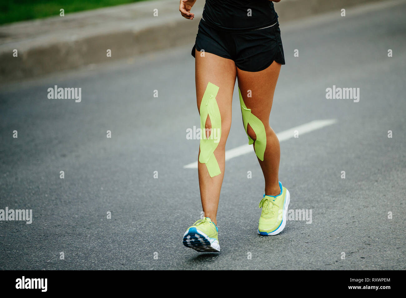 woman runner bright green kinesio tape on knees running on asphalt ...